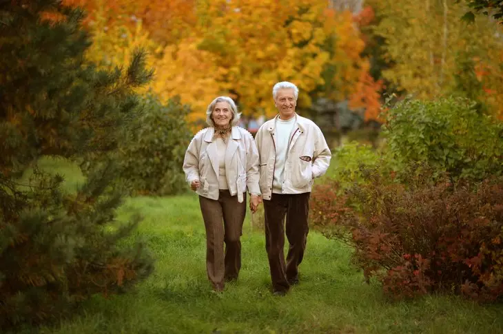 คู่สามีภรรยาสูงอายุเดินผ่านสวนสาธารณะในฤดูใบไม้ร่วง