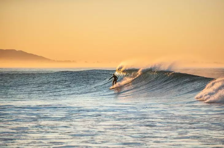 Surfer op enger Welle, géint e gëllenen Himmel