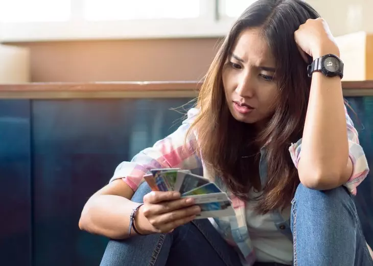 Wanita yang tampak sedih menatap segenggam kartu kredit.