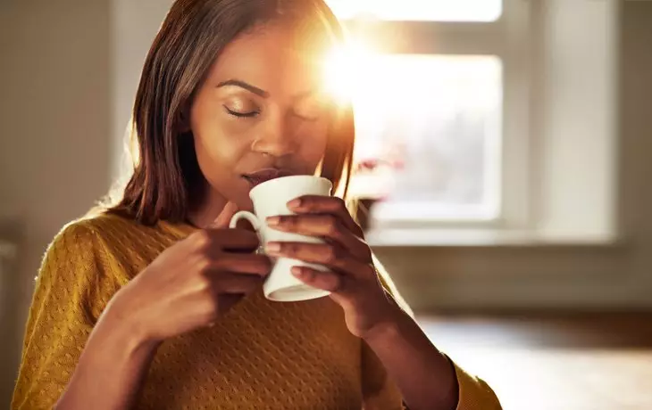 Una donna di colore si gode il caffè mentre sorge il sole del mattino