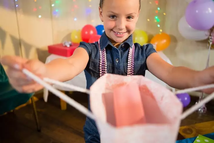 Ragazza alla festa di compleanno che porge il sacchetto del regalo.