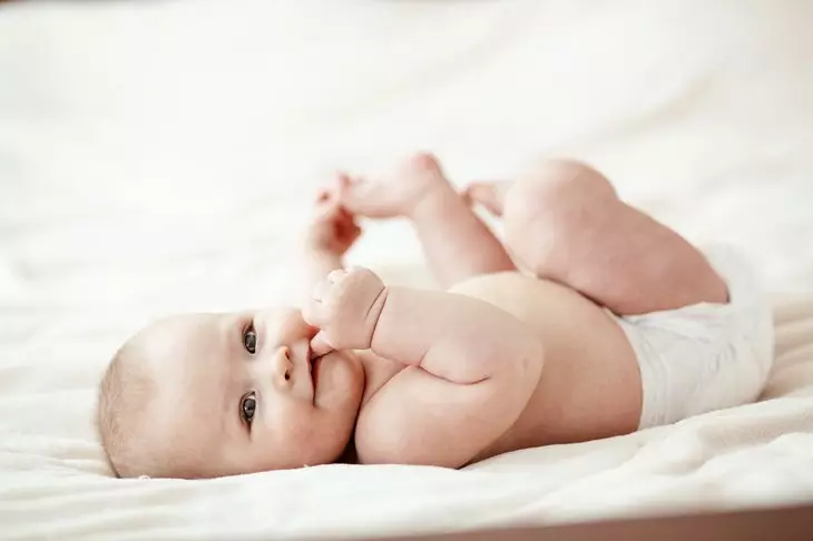 Bambino sorridente in pannolino, sdraiato sulla schiena.