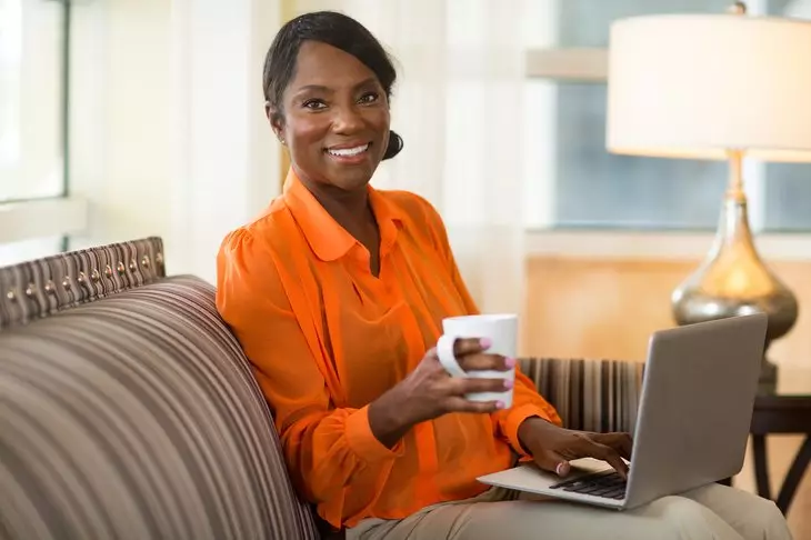 Wanita minum kopi dan menggunakan laptop di rumah