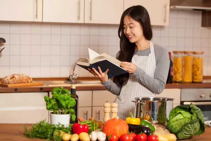 Wanita membaca buku masak di dapurnya