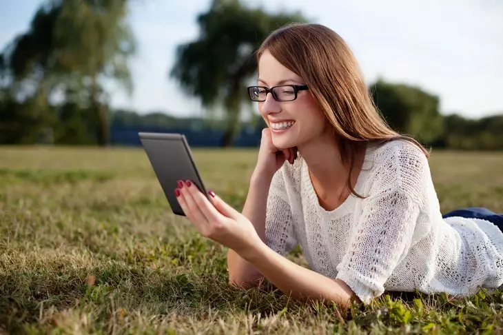 Owesifazane uyamamatheka ngenkathi ejabulela ukufunda i-e-book ku-e-reader futhi elele otshanini ngaphandle