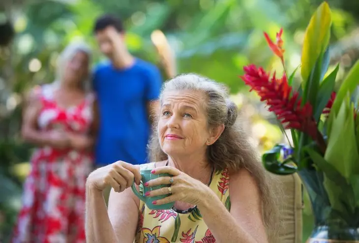 Eldre kvinne med en kopp kaffe i tropiske omgivelser.