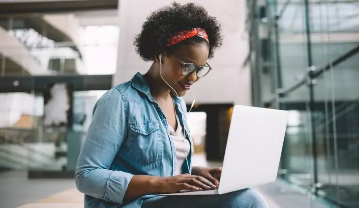 estudiante universitaria afroamericana sentada no portátil do campus