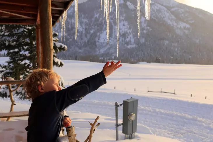 Bachgen yn cyrraedd am icicle, ar gyntedd caban ym mynyddoedd Utah