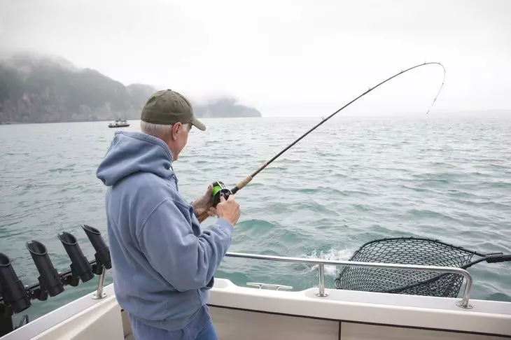 Senior man fiskjen fan in boat yn Alaskan wetters.