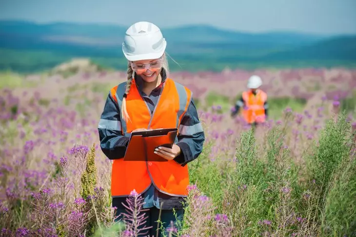 mujer científica portapapeles de casco investigando campo recultivado