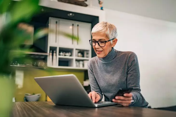 Mulher sênior trabalhando em casa no laptop e telefone