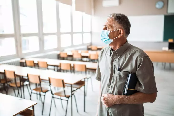 Professor mais velho usando uma máscara facial em uma sala de aula vazia