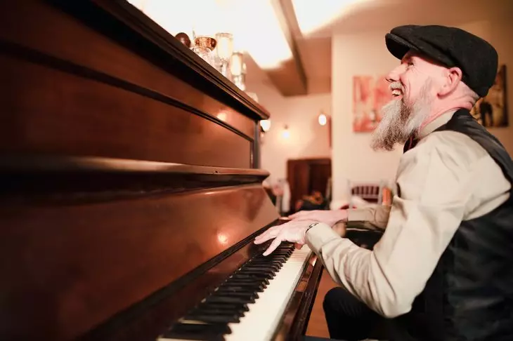 Um idoso barbudo de chapéu canta e toca música de piano