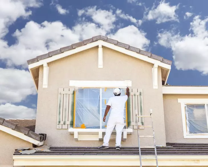 Pintor de casas ocupado pintando las molduras y las persianas de una casa.