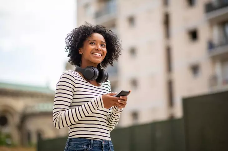 Owesifazane onama-headphone esebenzisa ifoni yakhe ngenkathi ehamba ngaphandle