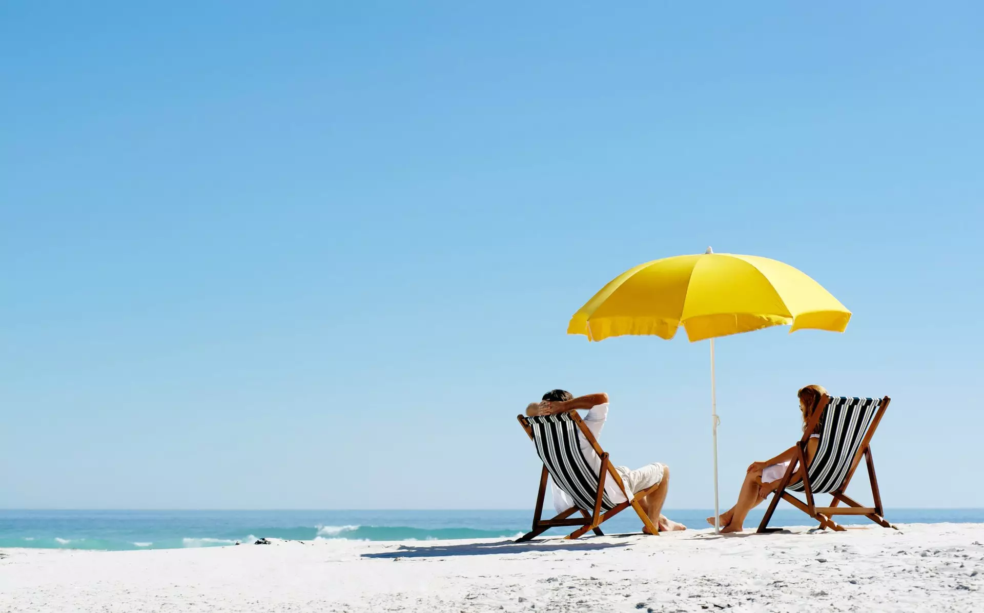 Paar sitzt am Strand unter Regenschirm