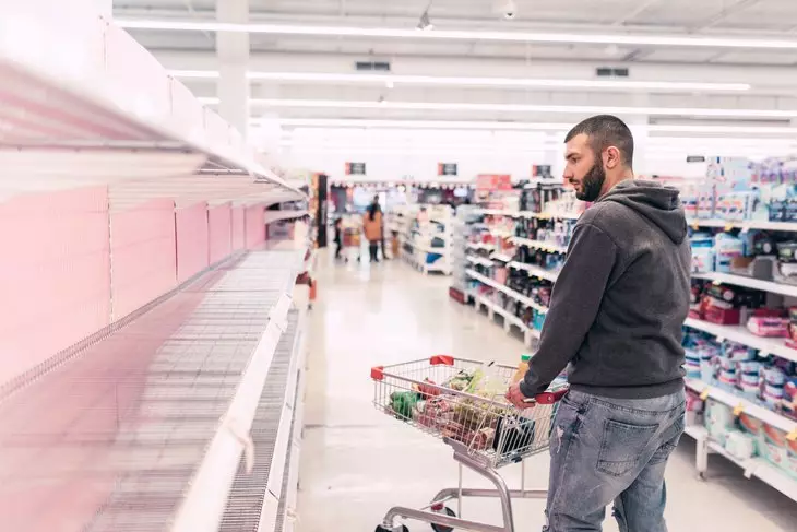 Un acquirente spinge un carrello attraverso un negozio con scaffali vuoti