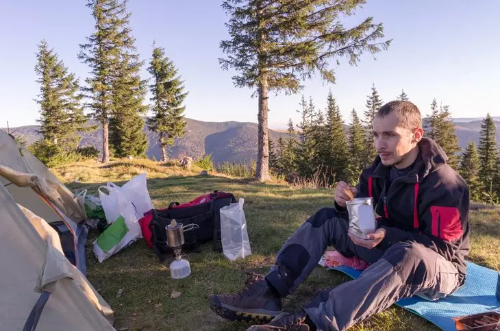 Un viaggiatore con lo zaino mangia cibo liofilizzato durante il campeggio