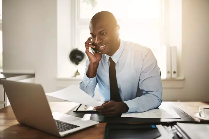 Ang isang itim na lalaki sa business attire ay nagtatrabaho sa isang laptop computer sa kanyang desk