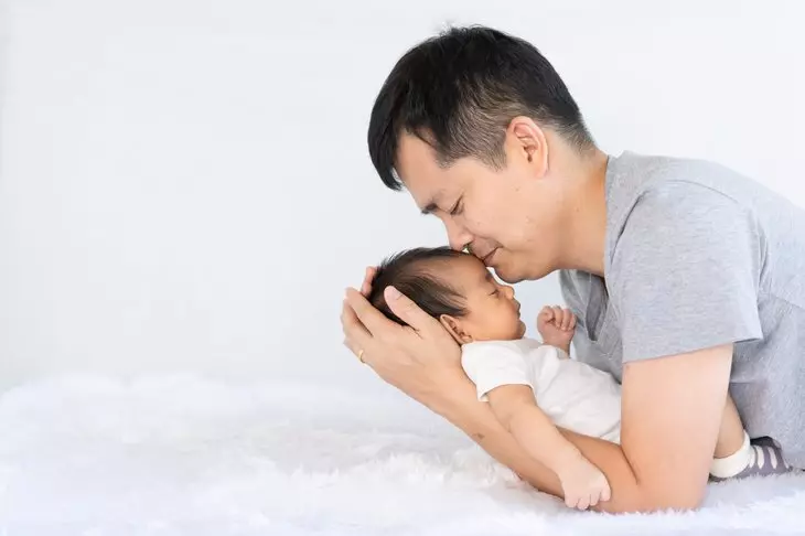 Potret close up ayah muda asia memegang dan mencium bayi laki-lakinya dengan momen kebahagiaan, fotografi dalam ruangan dengan konsep orang tua merawat dan mendukung anak mereka