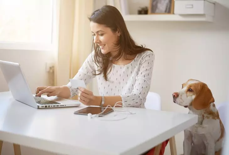 Uma mulher trabalha em um laptop em casa ao lado de seu cachorro