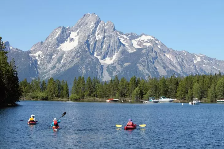 人們在湖上劃皮划艇，背景是一座山。