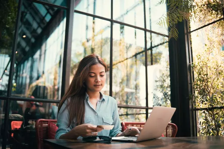 Jina Asyayî li ser laptopa xwe li qehwexaneyekê kirîna serhêl dike