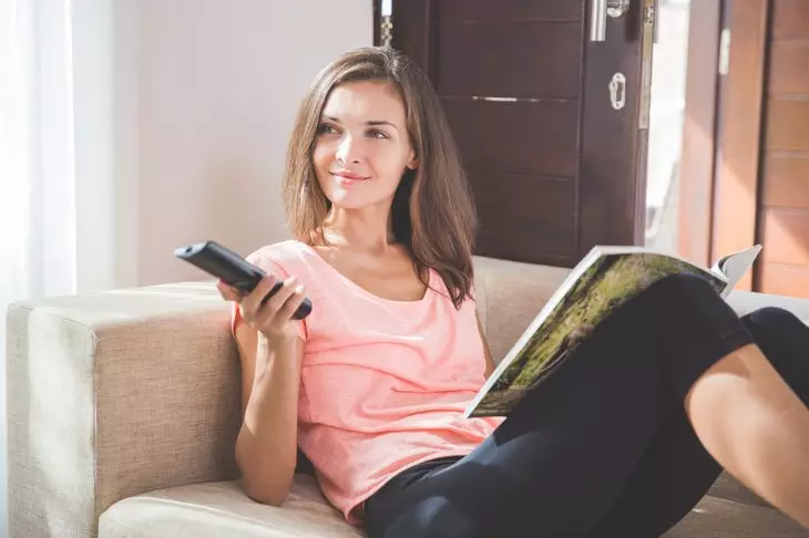 Mujer leyendo una revista y viendo la tele