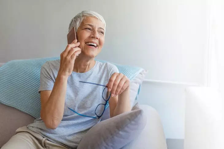 Ältere Frau, die an ihrem Handy spricht. Ältere Frau hat ein fröhliches Gespräch am Handy. Lächelnde ältere Frau, die zu Hause auf der Couch telefoniert. - Bild