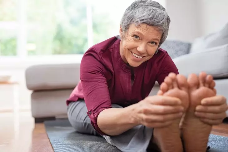 Eine Seniorin streckt sich beim Training zu Hause auf einer Yogamatte die Beine