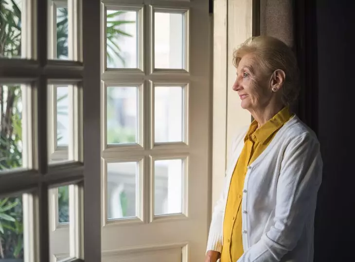 Eine ältere Frau schaut aus dem Fenster ihres Hauses