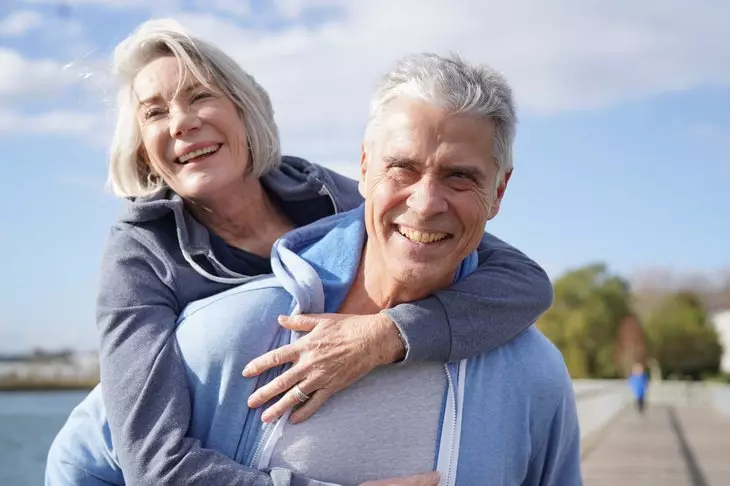 E gléckleche Senior Mann gëtt senger Fra e Piggyback Ride dobaussen