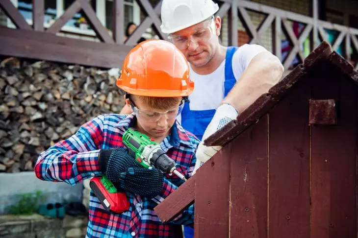 Far og sønn bygger et hundehus med drill og har på seg konstruksjonshjelmer