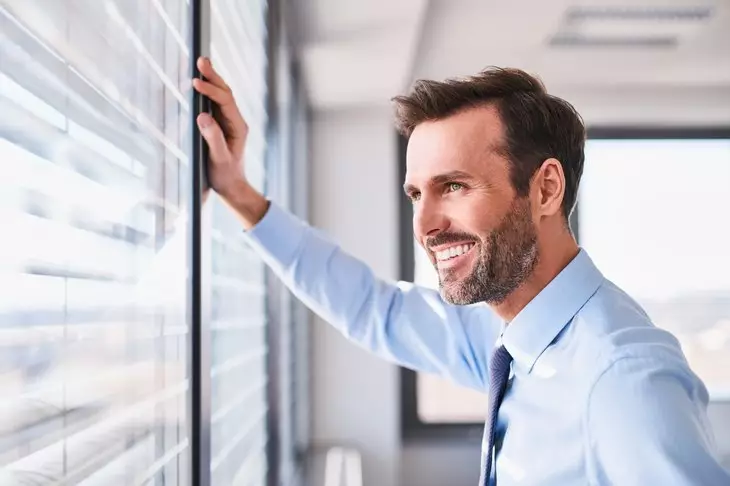 Glücklicher Geschäftsmann im Büro, der aus dem Fenster schaut