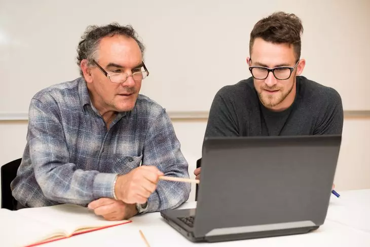 Profesor y asistente trabajando en una laptop.