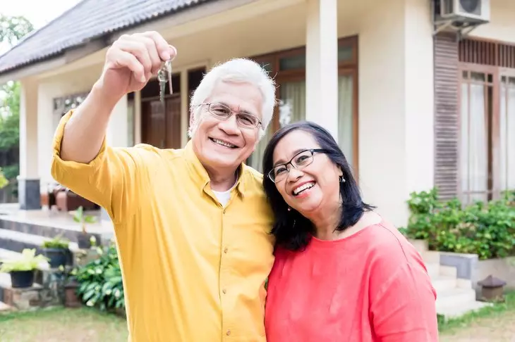 Pasangan tua yang bahagia di depan rumah yang mereka beli atau jual