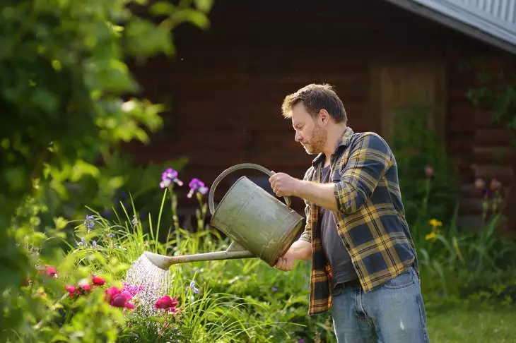Muž zalévá květiny na svém dvoře